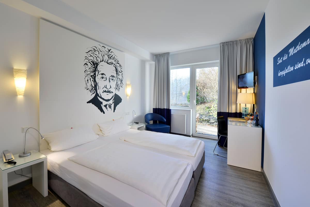 Quarto de hotel com duas camas, uma escrivaninha, uma cadeira, uma televisão e uma grande obra de arte na parede.