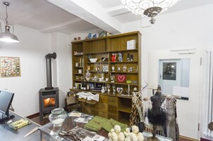 Quarto aconchegante com estante de madeira, mesa com diversos objetos, lareira e janela com vista.