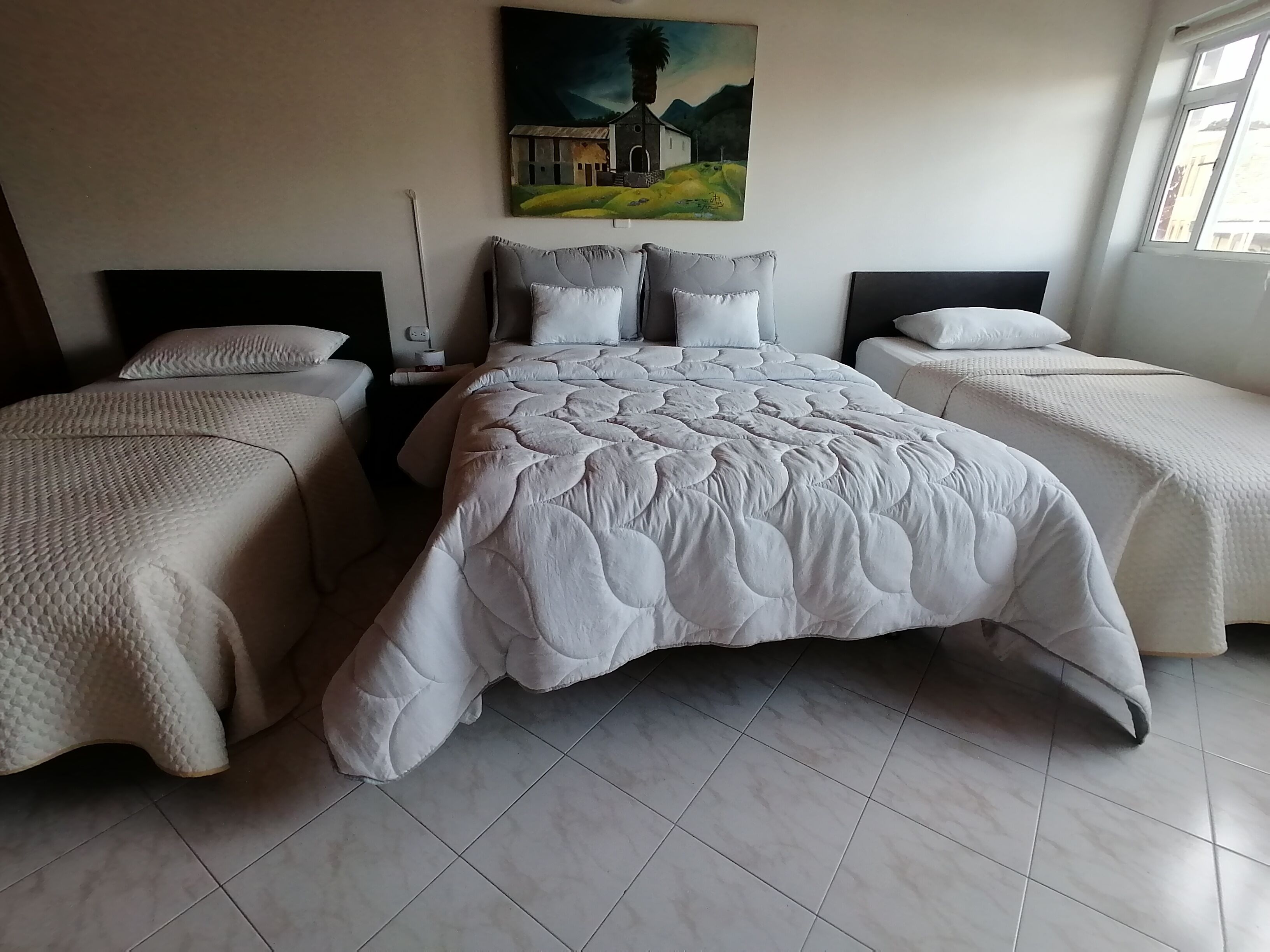 Quarto de hotel com uma cama grande, duas camas menores e um quadro na parede.