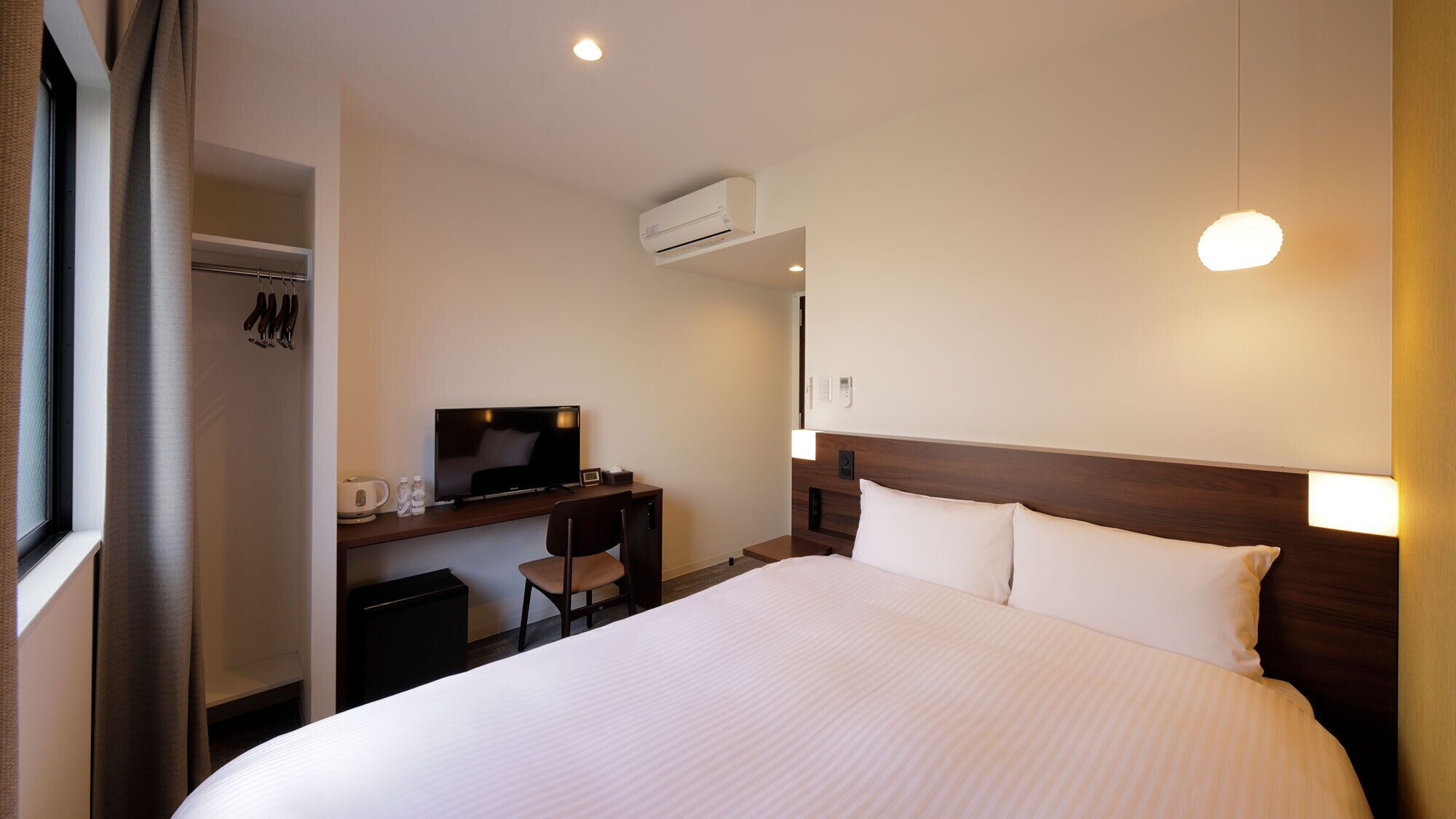 Quarto de hotel com cama, escrivaninha, televisão, cabideiro e ar condicionado.