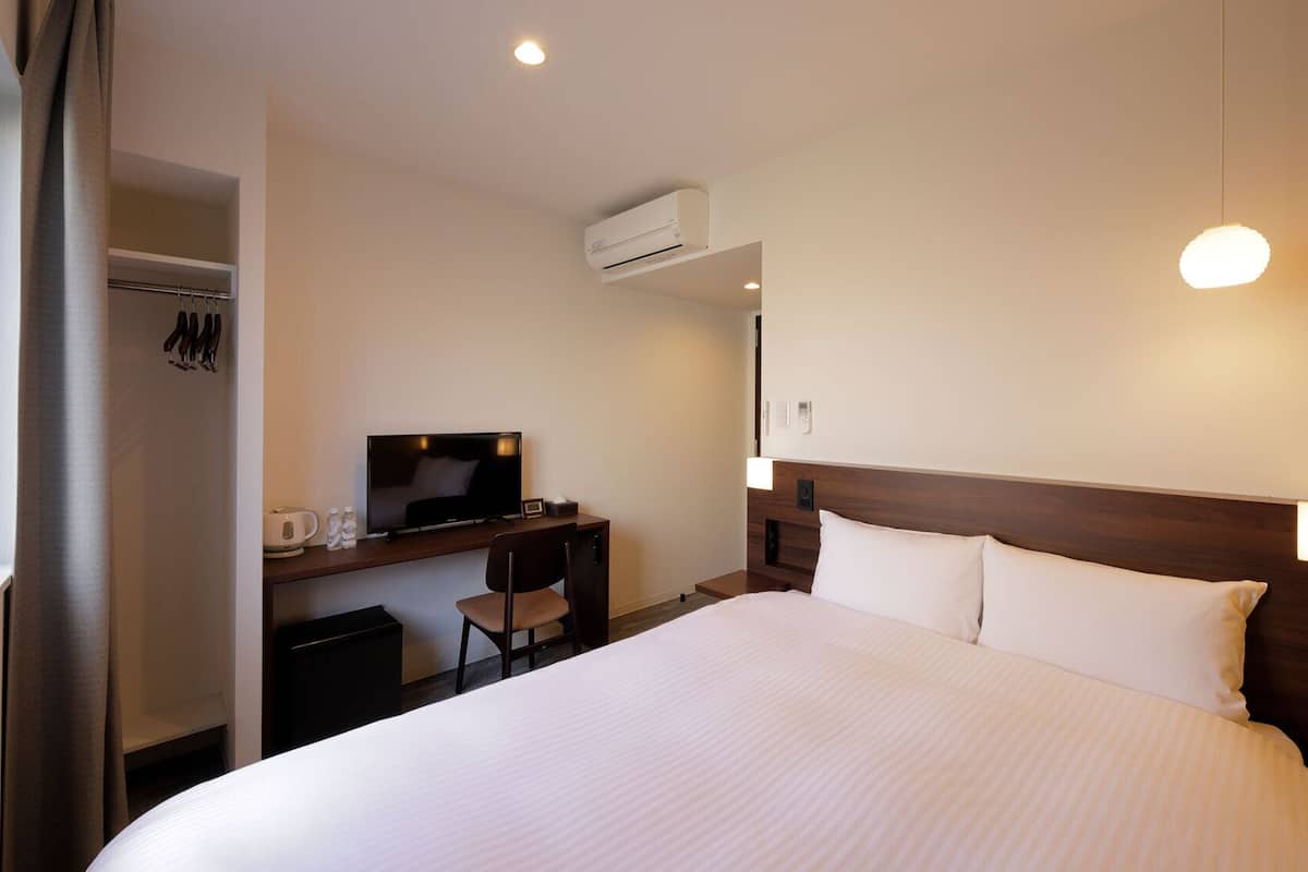 Quarto de hotel com cama, escrivaninha, televisão, cabideiro e ar condicionado.