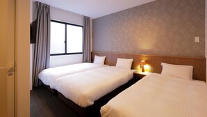 Quarto de hotel com duas camas, uma televisão fixada na parede, uma janela com cortinas e um papel de parede estampado.