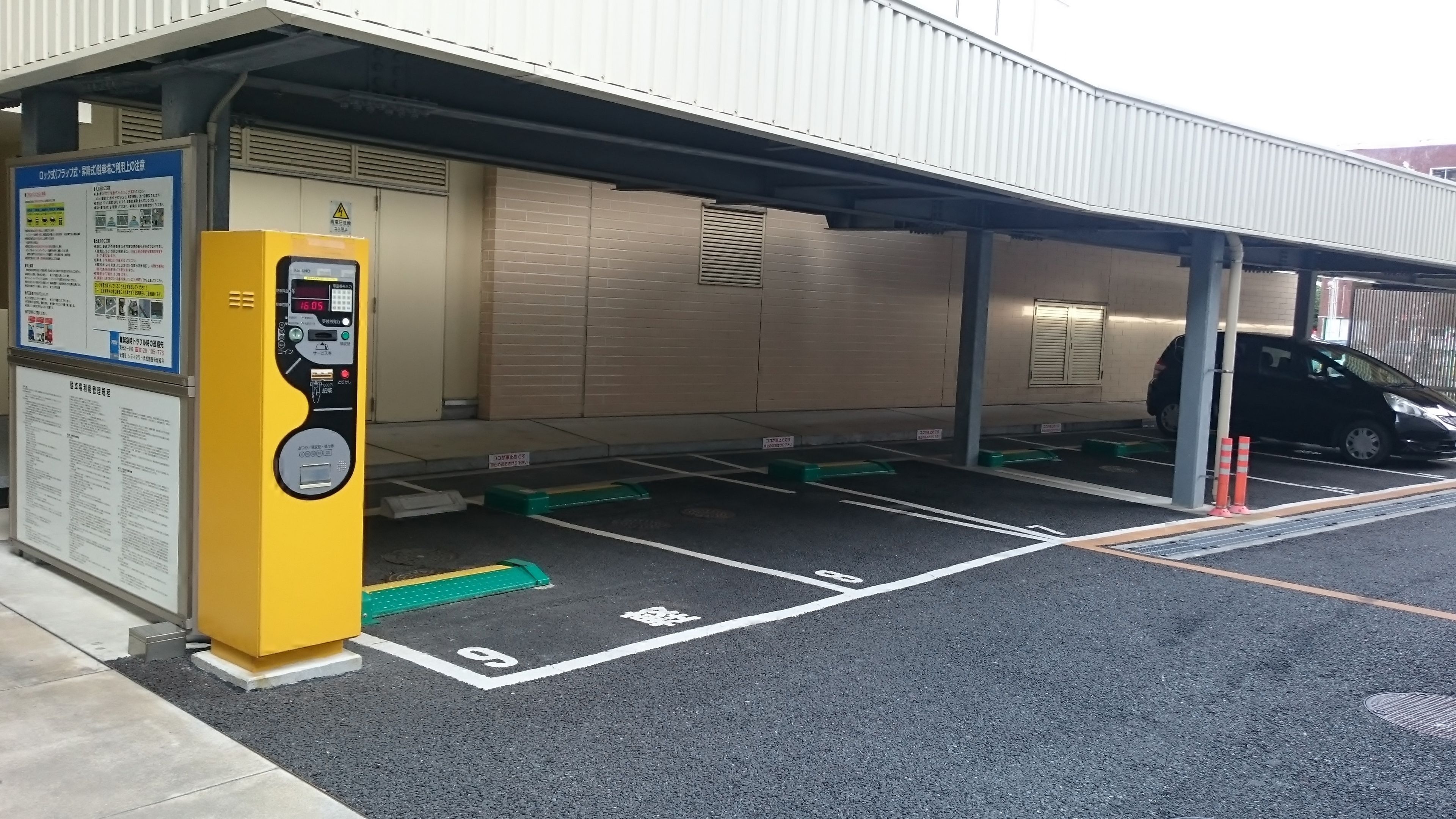 Garagem de estacionamento com parquímetro amarelo, vagas demarcadas e um carro preto dentro.