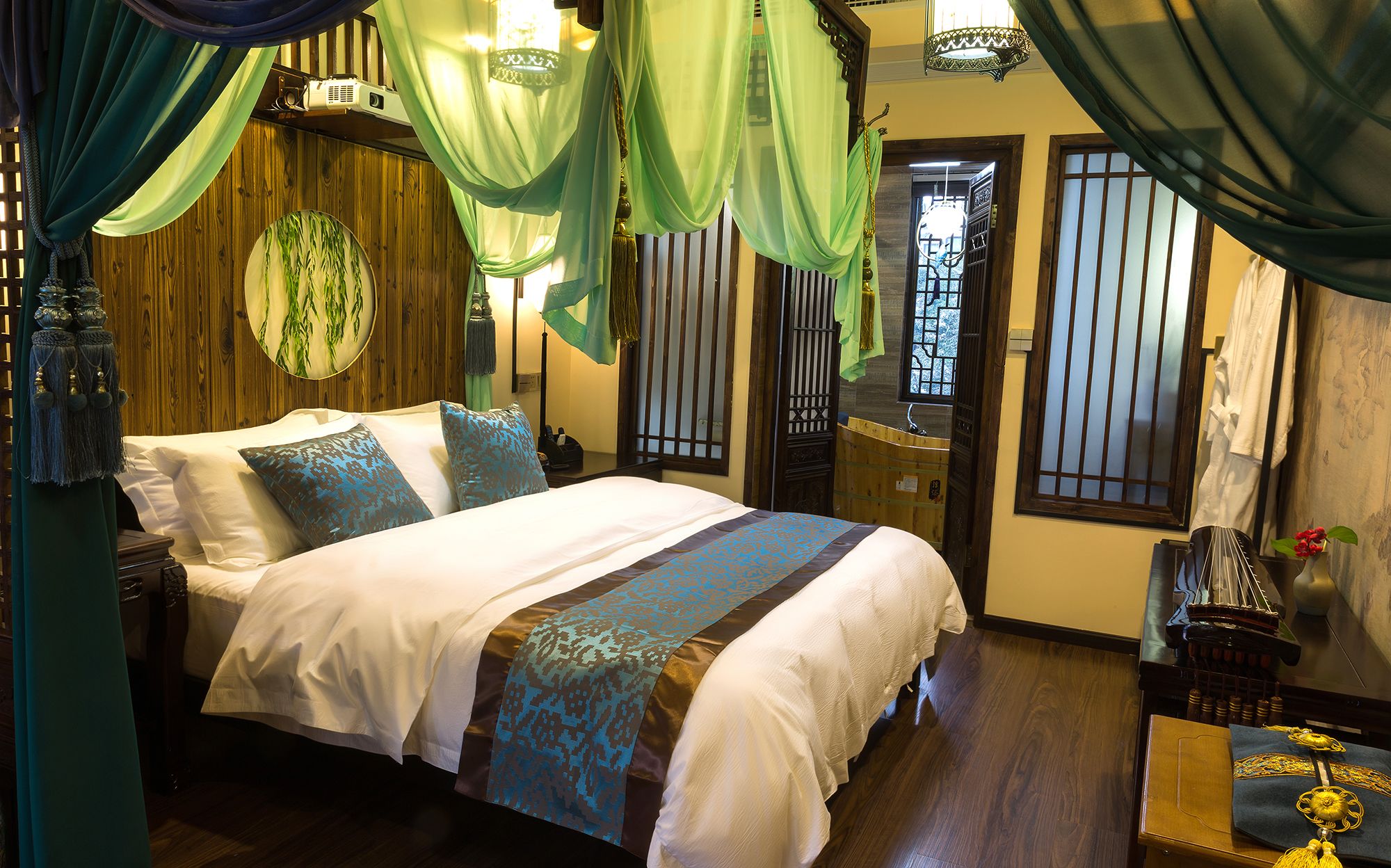 Quarto tradicional com cama, cortinas, cabeceira de madeira, mesa de cabeceira e uma pequena mesa com um objeto decorativo.