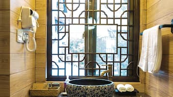 Um banheiro com decoração em madeira, uma janela ampla com grades metálicas decorativas, uma pia com uma bacia ornamental, um secador de cabelo e um porta-toalhas.