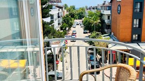 Varanda com cadeira de vime, vista para uma rua com carros estacionados e edifícios.