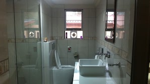 Casa de banho com chuveiro envidraçado, sanita e lavatório com espelho em cima.