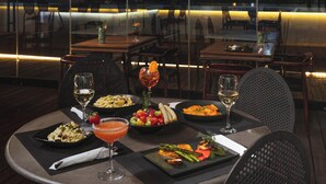 Uma mesa de restaurante com pratos de comida, copos de vinho e um cocktail.