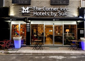 The Corner Inn Hotels by Suit, com fachada moderna, entrada de vidro e área de estar externa.