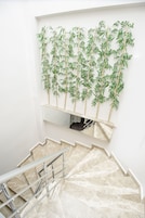 Uma escadaria com degraus de mármore bege e corrimão de metal, que conduz a uma parede branca com painel de plantas de bambu.