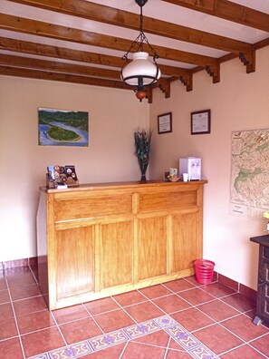 Uma receção com acabamento em madeira, um candeeiro pendente, um mapa emoldurado na parede e um chão em azulejos com uma moldura decorativa.