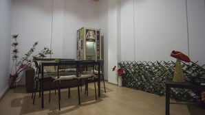 Uma área de refeições com mesa e cadeiras de madeira, um sofá, uma planta decorativa e uma pequena mesa com um objeto dourado.