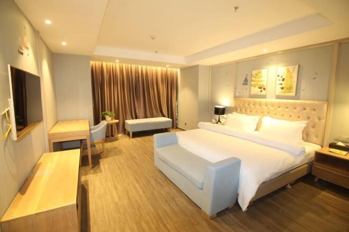 Quarto de hotel com uma cama grande, uma escrivaninha, um banco e uma televisão.