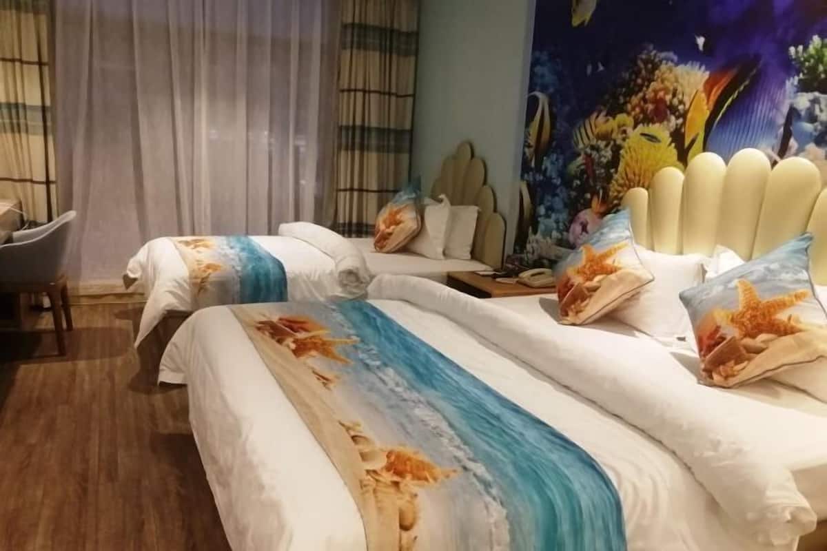 Quarto de hotel com duas camas, cada uma com colcha branca com cena de praia. Há uma pintura grande de vida marinha na parede atrás das camas.