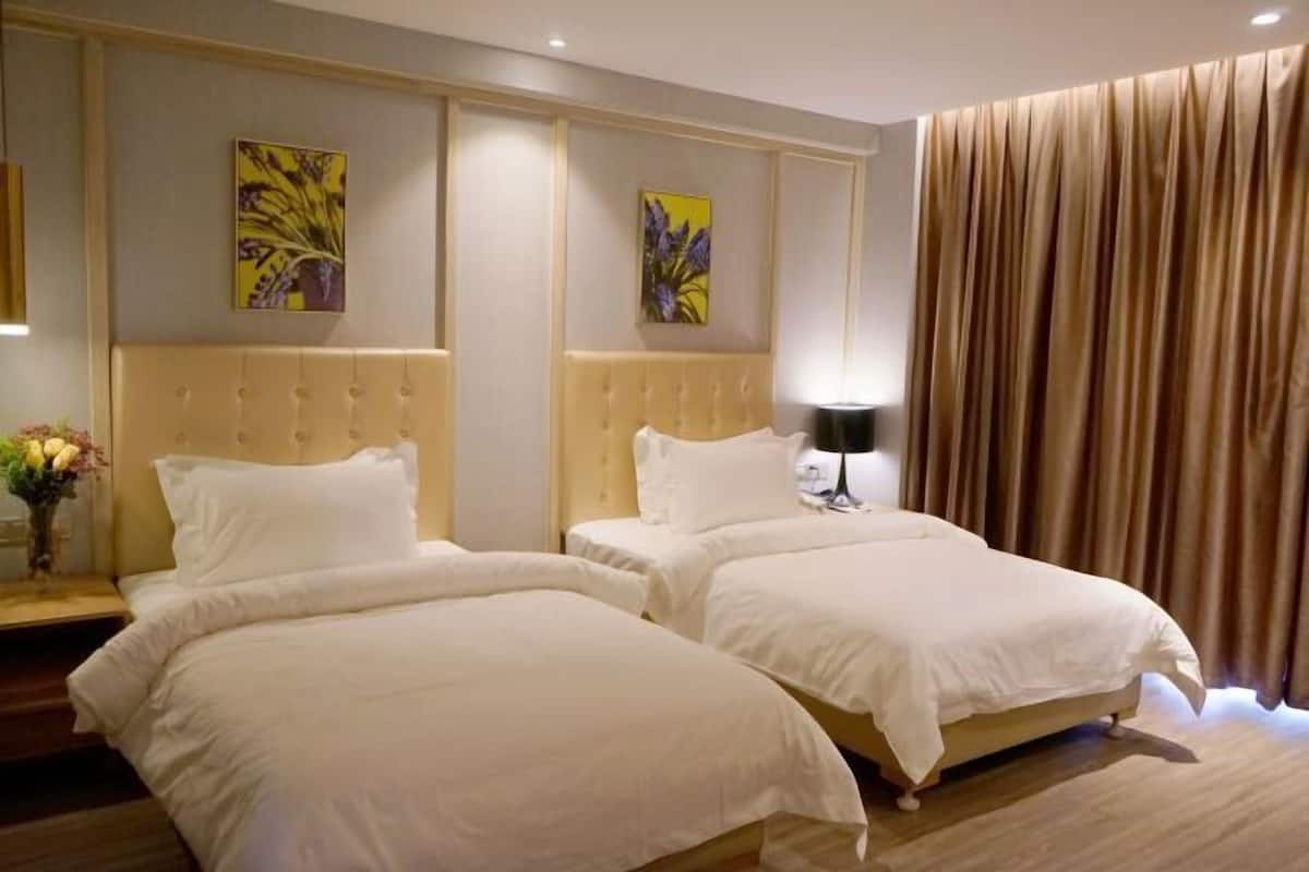 Quarto de hotel com duas camas, uma janela grande com cortinas e obras de arte nas paredes.