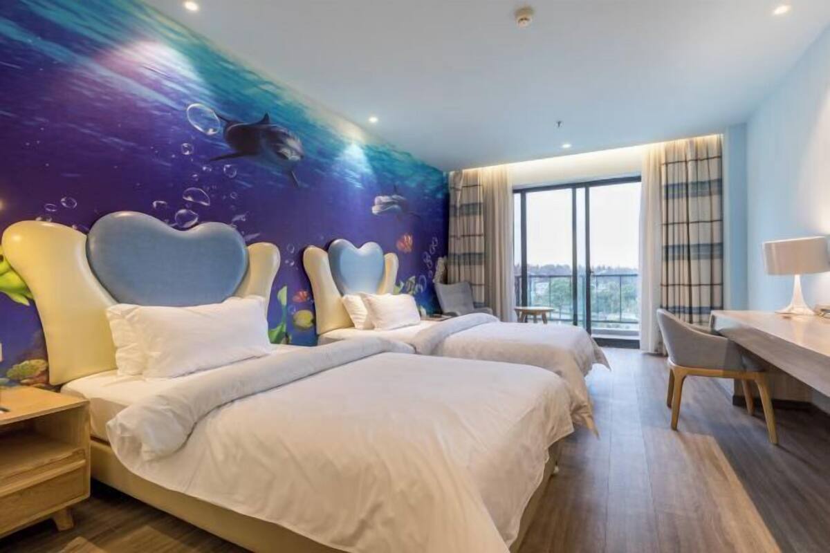 Quarto de hotel com duas camas, uma escrivaninha e uma janela grande.
