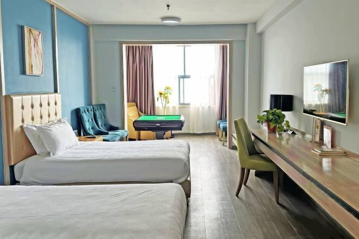 Quarto de hotel com duas camas, uma mesa de escritório com televisão, mesa de bilhar e vista para o exterior.