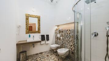 Uma casa de banho com uma pia branca, sanita, bidé, cabine de duche em vidro e azulejos com padrão.