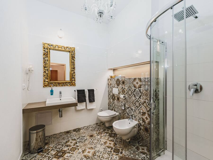Uma casa de banho com uma pia branca, sanita, bidé, cabine de duche em vidro e azulejos com padrão.