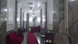 Um hall de entrada com paredes de mármore, um tapete vermelho e um balcão de recepção.