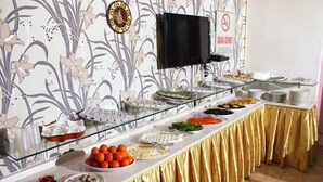 Uma mesa de buffet com diversos alimentos e uma televisão fixada na parede.