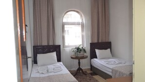 Quarto de hotel com duas camas de solteiro, uma mesinha com uma planta e uma janela com cortinas.
