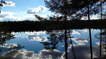 Um lago tranquilo com reflexos de árvores e nuvens, rodeado por uma floresta.