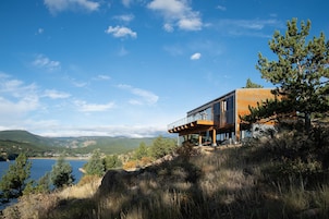 Uma casa moderna com varanda com vista para um lago e montanhas.