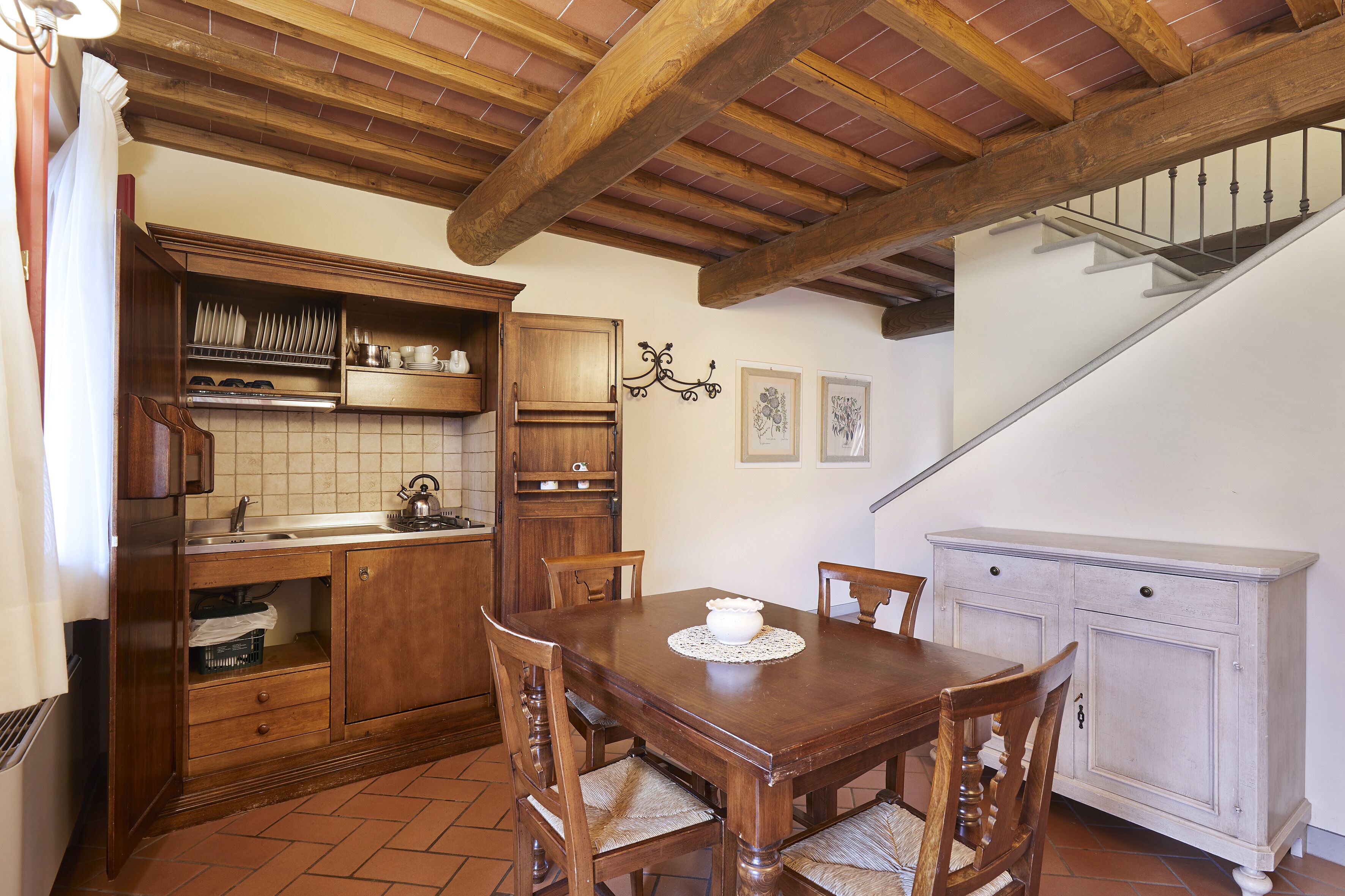 Uma cozinha tradicional com armários de madeira, uma mesa de jantar e uma escada.
