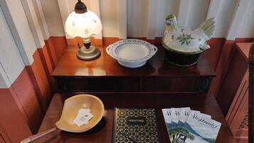 Uma mesa de madeira com uma lâmpada, um prato decorativo, uma cesta, uma tigela, um livro intitulado 'Visitors' e panfletos.