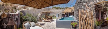 Área de piscina com parede de pedra, cadeira suspensa e estrutura de telhado de palha.