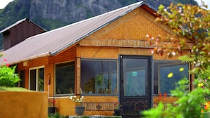 Uma cabana de madeira com telhado inclinado, janelas grandes e uma porta com uma placa verde.