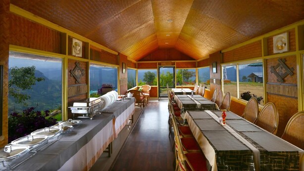 Uma sala de jantar com mesas compridas, cadeiras e vista para o exterior.