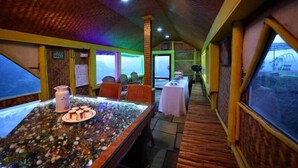 Uma área de jantar acolhedora, com uma mesa posta para dois, teto de madeira e vista pela janela.