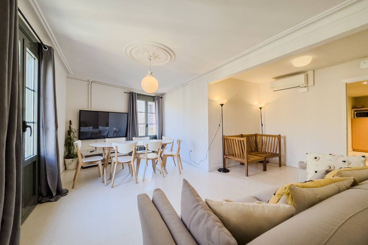 Uma sala de estar moderna com sofá, área de jantar com cadeiras e mesa, televisão e luminária no teto.