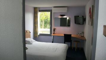 Quarto de hotel com cama, escrivaninha, cadeira, televisão e janela com cortinas.
