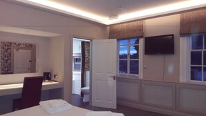 Quarto de hotel com uma cama, televisão fixada na parede, janela com cortinas e porta para uma varanda.