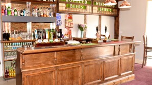 Uma área de bar com balcão de madeira, várias garrafas, copos e um letreiro com a inscrição 'BOTTLED BEERS WINE AND SPIRITS'.