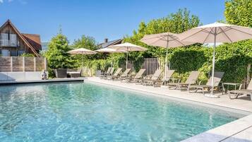 Piscina com espreguiçadeiras e guarda-sóis, cercada por um muro de madeira e vegetação.