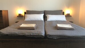 Uma cama de casal com colcha cinza texturizada, duas almofadas brancas e duas luminárias de cabeceira.