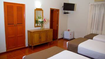 Quarto de hotel com duas camas, um guarda-roupa de madeira, televisão na parede e uma pequena mesa com um vaso de flores.