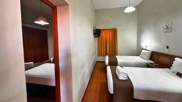 Quarto de hotel com duas camas, televisão, piso de madeira e janela com cortinas.