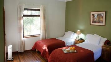 Quarto com duas camas, uma janela com cortinas, uma mesa de cabeceira com abajur e um quadro na parede.