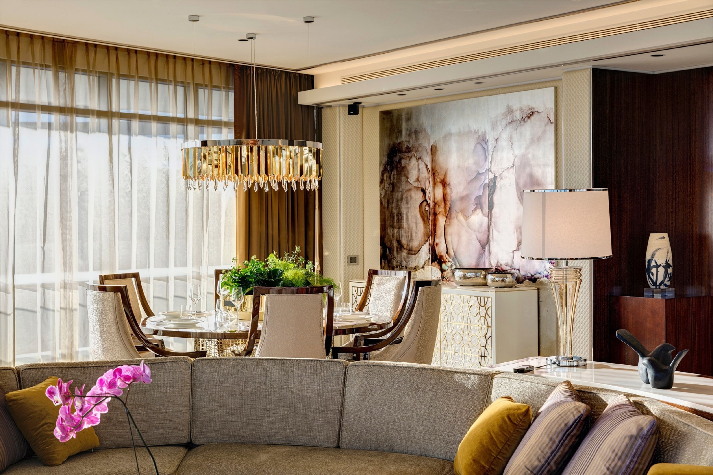 Um lobby de hotel moderno com área de refeições, uma grande pintura abstrata e um candelabro.