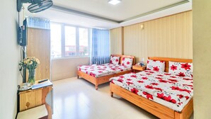 Quarto com duas camas de madeira, uma escrivaninha com abajur e uma janela com cortinas.