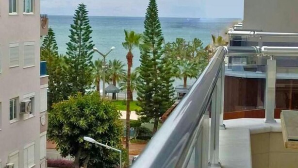 Uma varanda com vista para o mar, cercada por vegetação e edifícios.