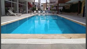 Piscina com espreguiçadeiras e guarda-sóis, rodeada por edifícios modernos.