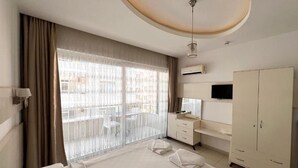 Quarto de hotel com cama, escrivaninha, armário e televisão.