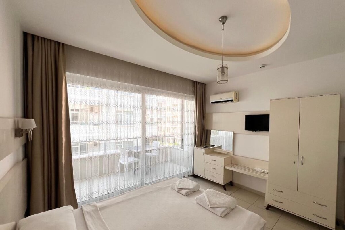 Quarto de hotel com cama, escrivaninha, armário e televisão.