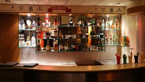 Uma área de bar com prateleiras cheias de garrafas de bebidas e copos, um balcão com um cardápio e uma placa indicando o nome do bar.